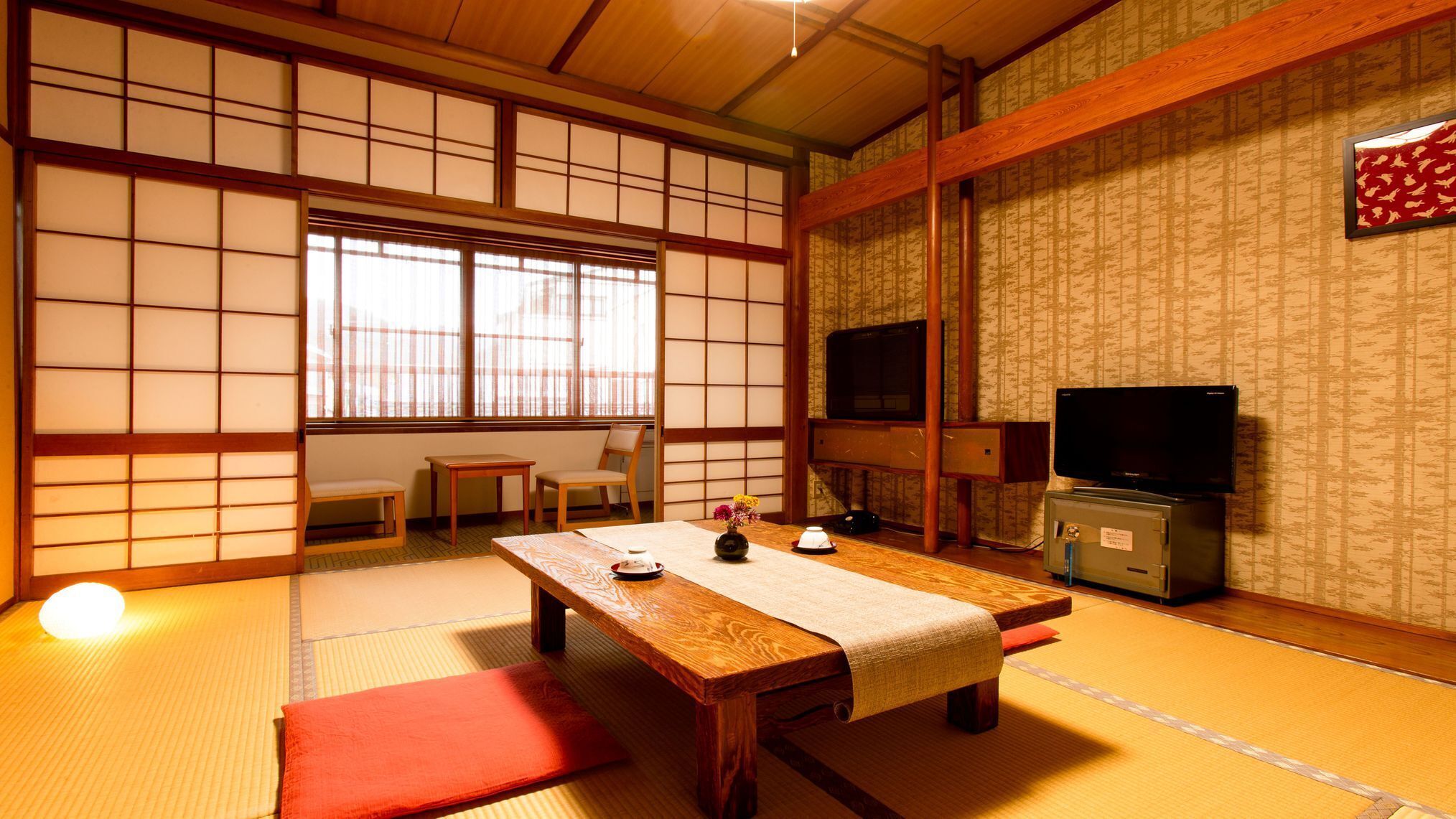 Um quarto japonês tradicional com tatames, uma mesa de madeira baixa, uma televisão e uma porta de correr.