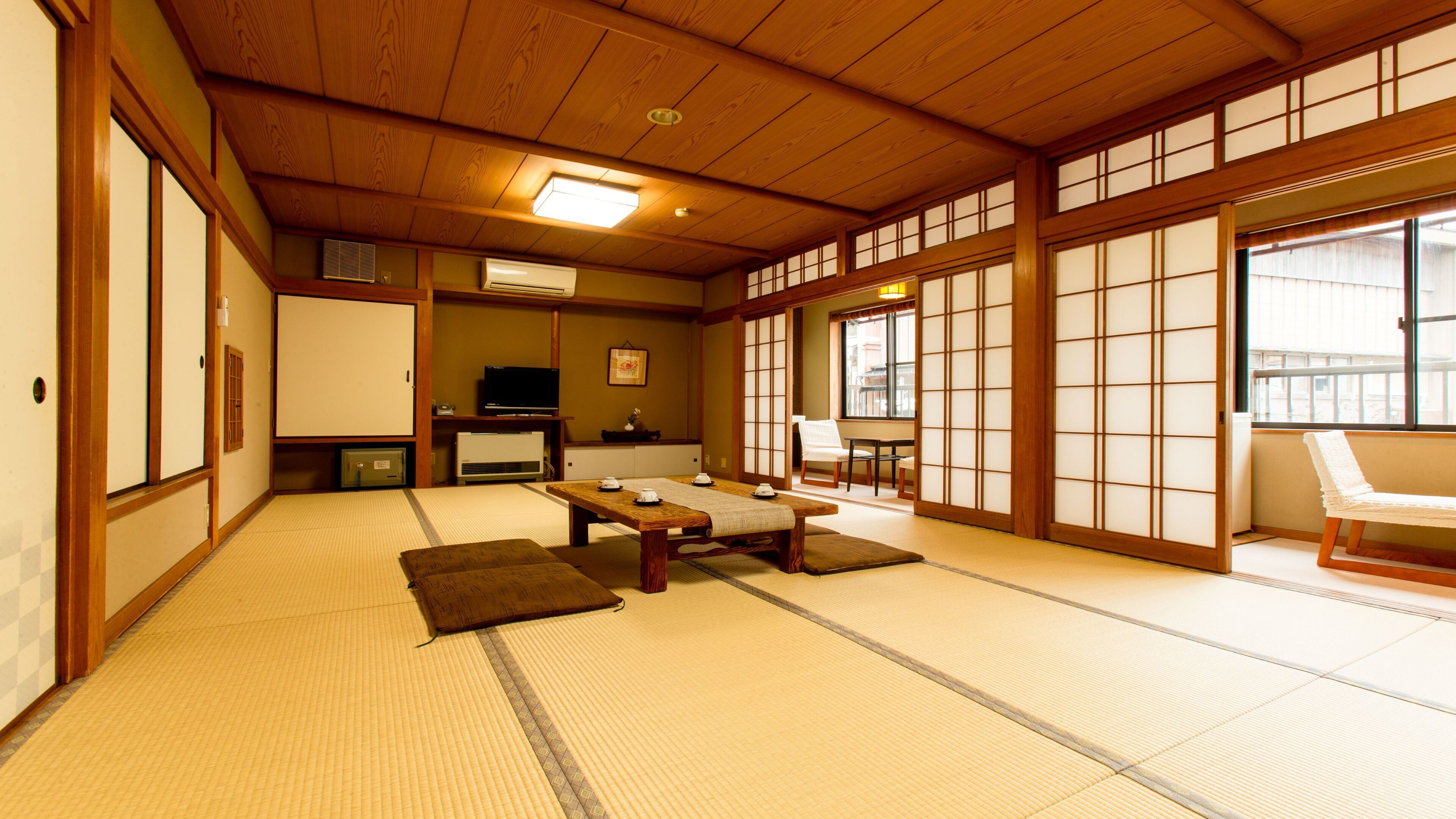 Um quarto japonês tradicional com tatames, uma mesa baixa com almofadas, portas deslizantes e uma televisão.