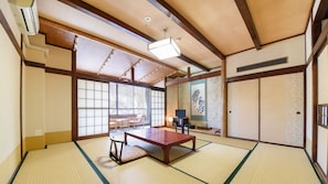 Um quarto japonês tradicional com piso de tatame, uma mesa baixa, televisão e portas corrediças.