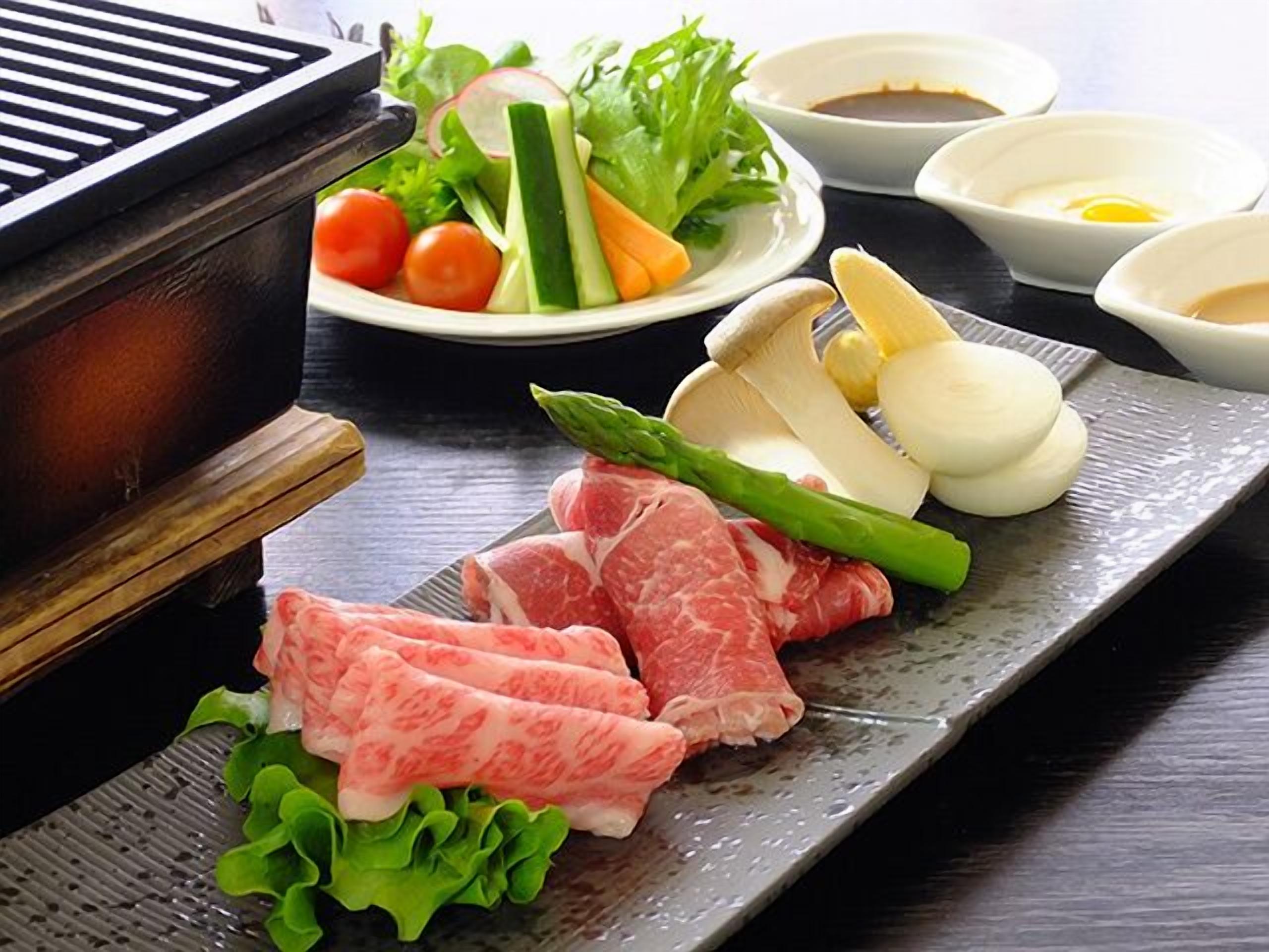 Uma chapa quente com diversos tipos de carne, legumes e acompanhamentos.