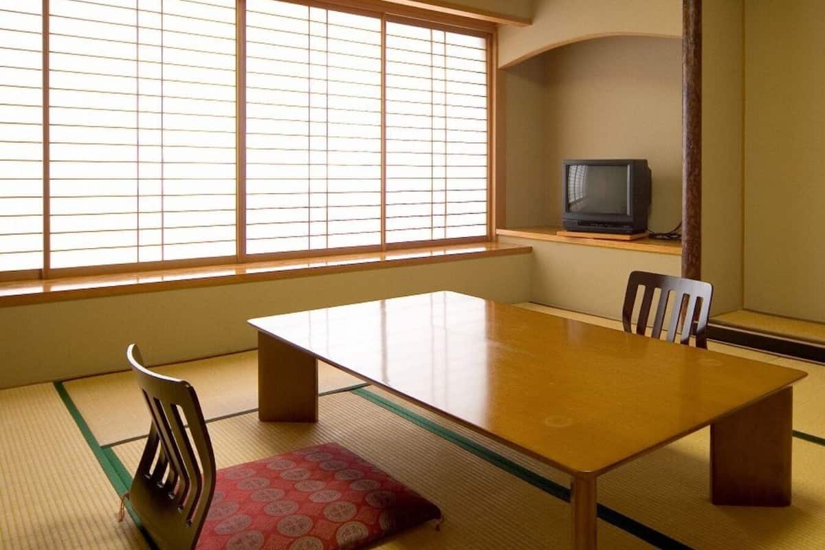 Um espaço com tatames, uma mesa de madeira, cadeiras, uma televisão e um quadro na parede.