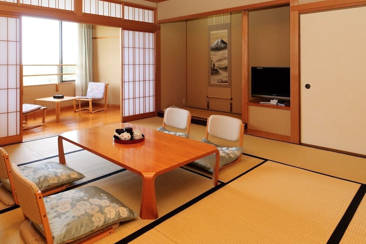 Um quarto japonês tradicional com tatames, uma mesa de madeira baixa e uma televisão.