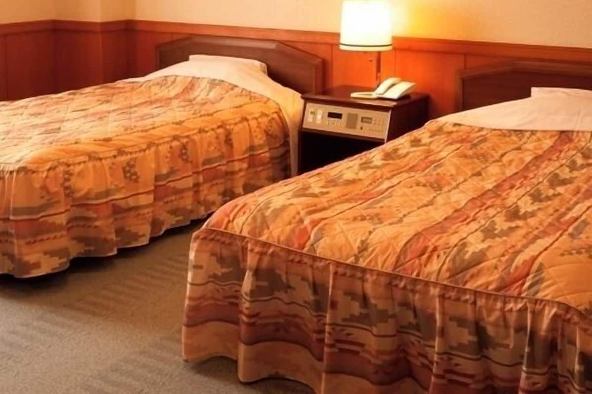Duas camas com roupa de cama estampada, uma luminária de mesa, um relógio e um quadro na parede.
