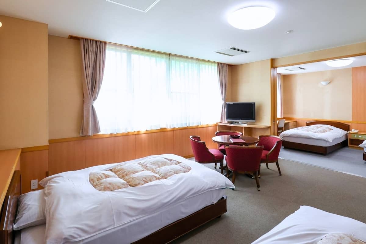 Quarto de hotel com duas camas, televisão, mesinha e uma cadeira.