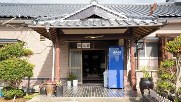 Um edifício tradicional japonês com telhado de telhas, uma placa de identificação e um refrigerador azul na parte externa.
