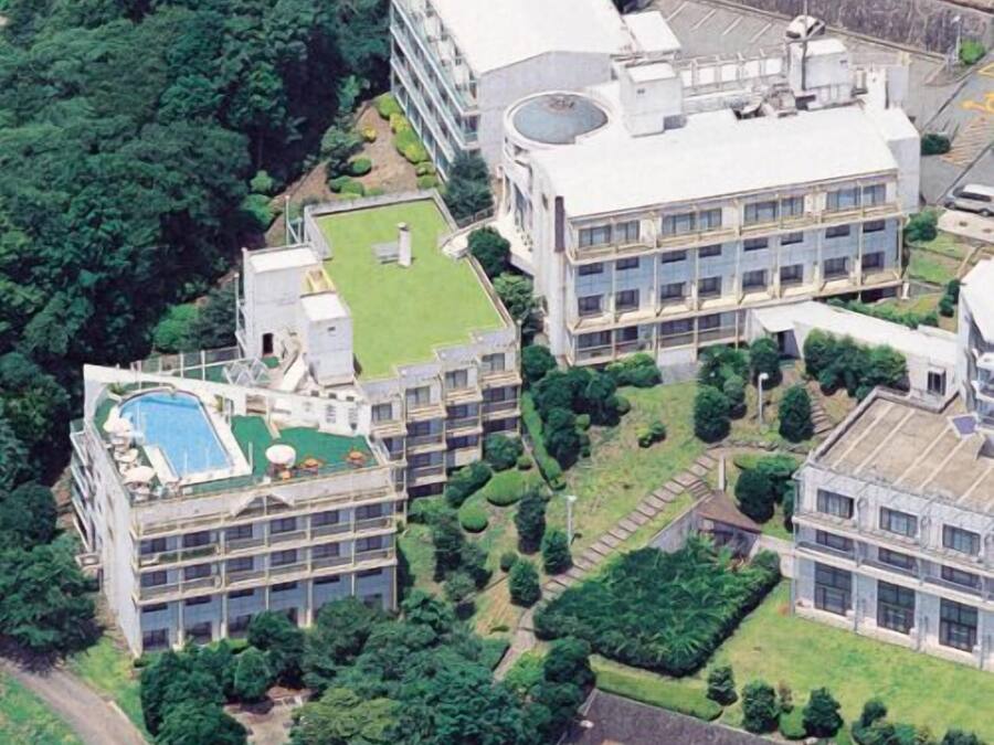 Um edifício de vários andares com piscina no terraço, cercado por áreas verdes e estacionamento.