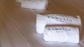 Cama com toalhas dobradas com cuidado, identificadas com 'KANALIA', e parede de pedra ao fundo.
