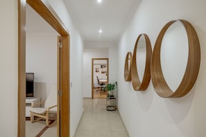 Um corredor com moldura de porta de madeira, uma cadeira branca, um vaso com planta e três espelhos de parede em madeira.