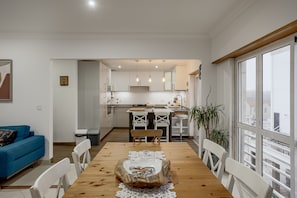 Uma cozinha moderna com armários brancos, uma mesa de jantar com um arranjo central e vista para o exterior através de grandes janelas.
