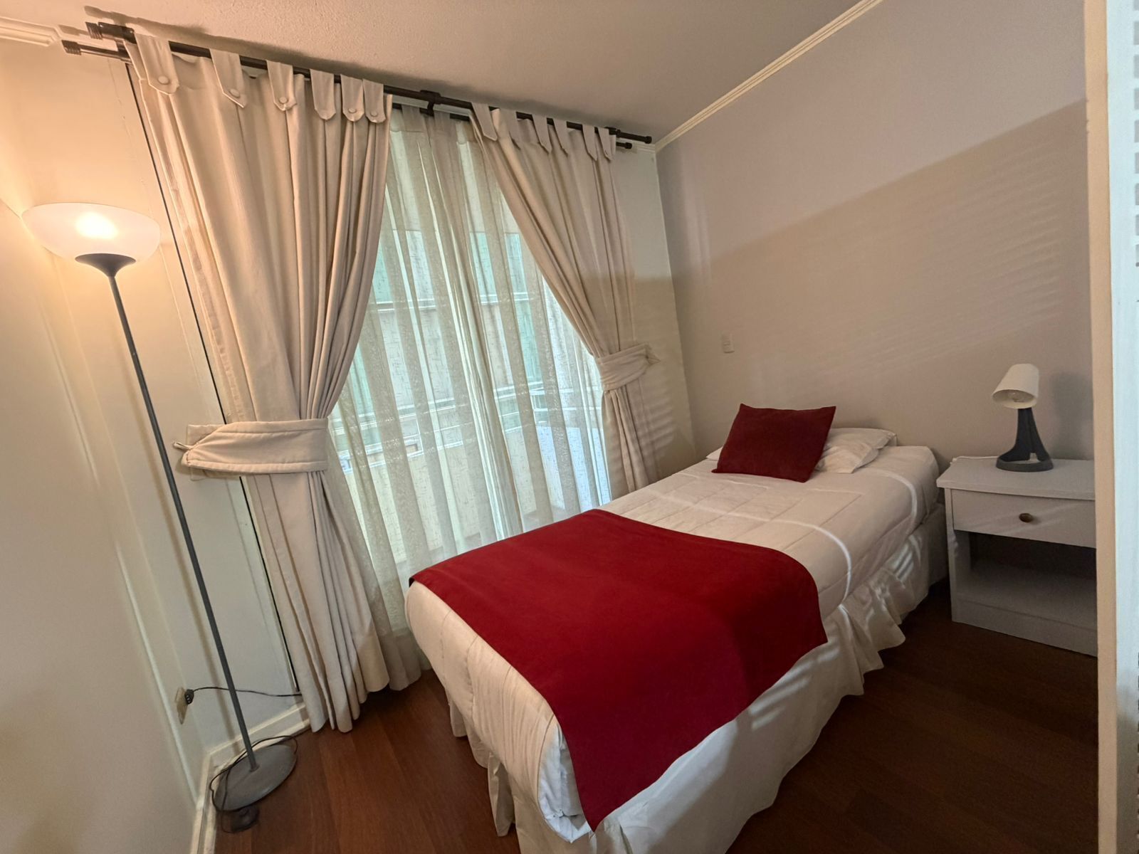 Quarto com cama, mesa de cabeceira, abajur e luminária de chão.
