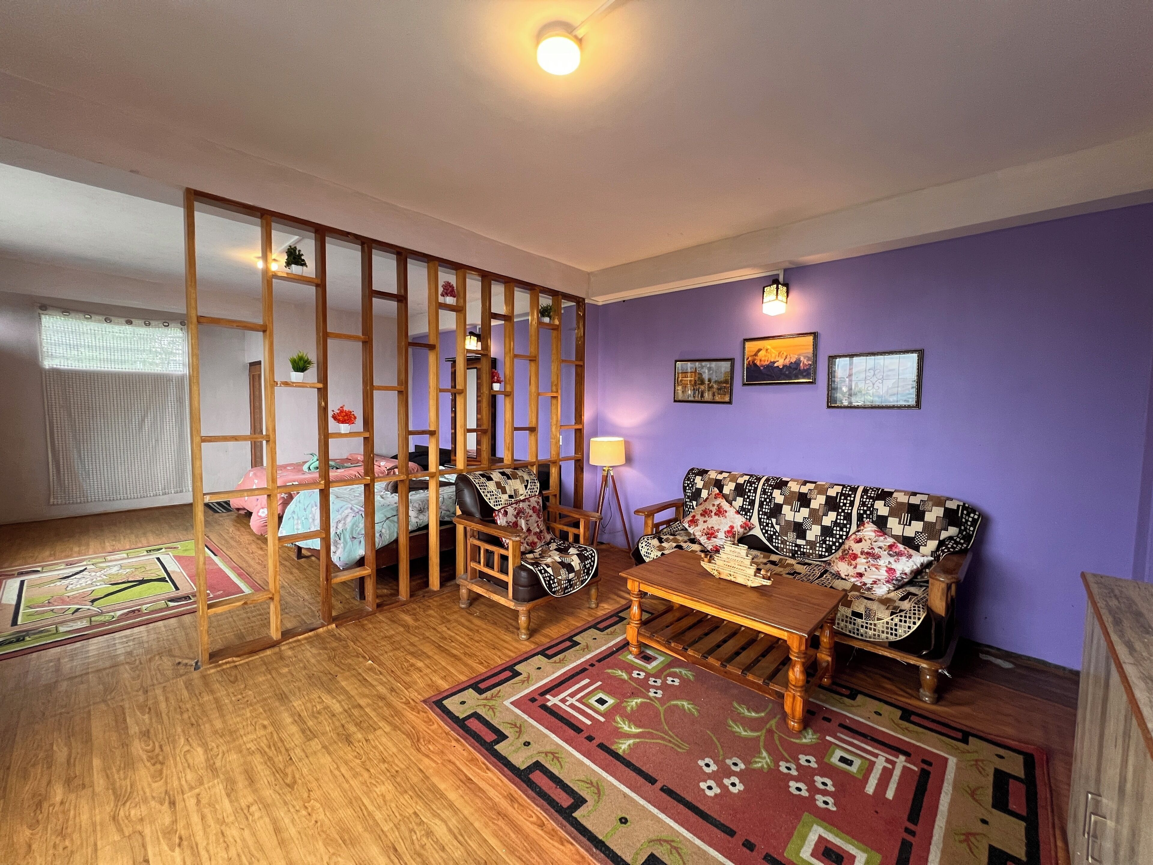 Quarto com divisória de madeira, sofá, mesa e cama com roupa de cama florida.