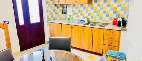 Uma cozinha com armários de madeira, painel de azulejos, pia e mesa de jantar com cadeiras.