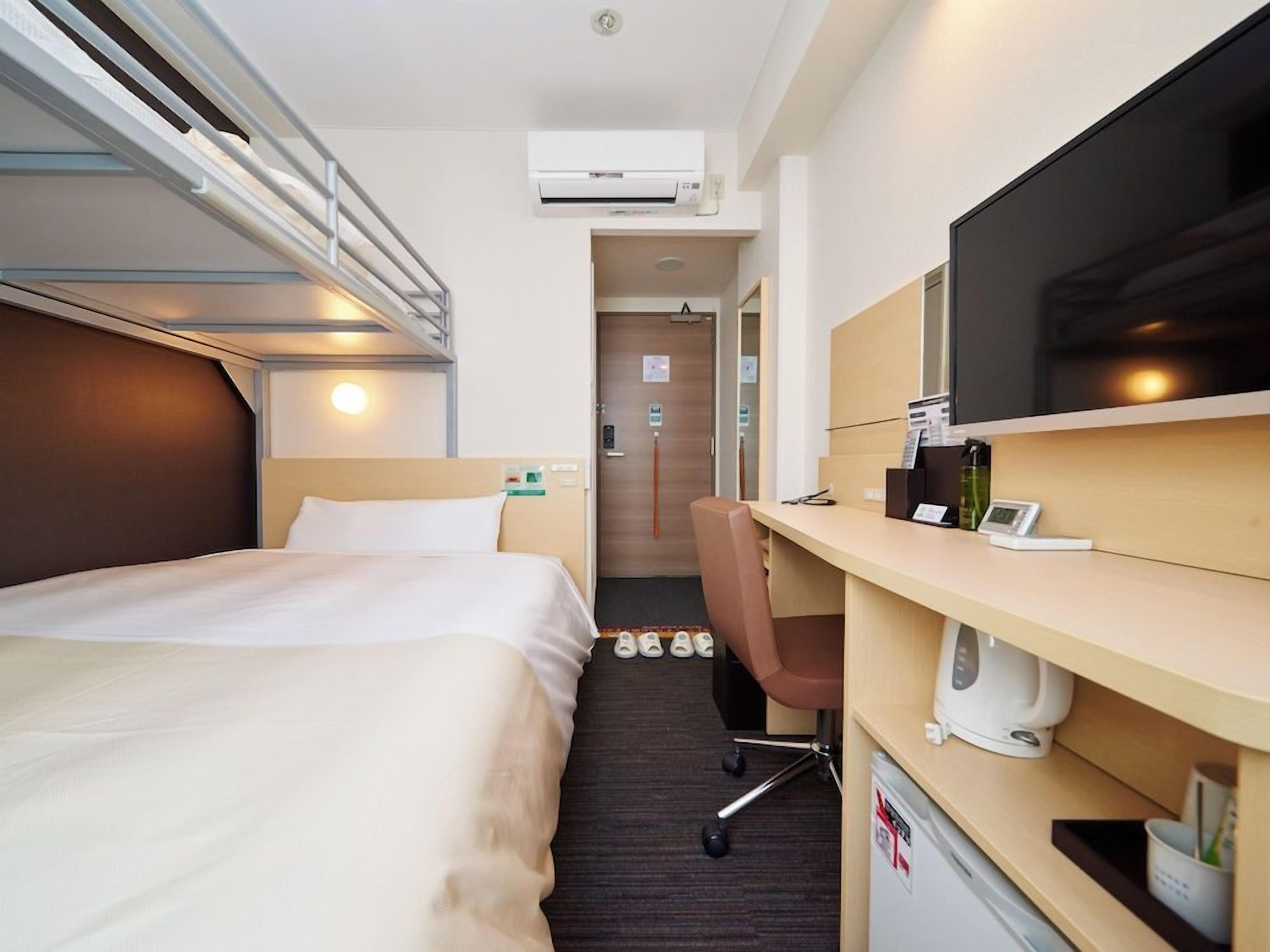 Quarto de hotel com cama, escrivaninha, cadeira e televisão.