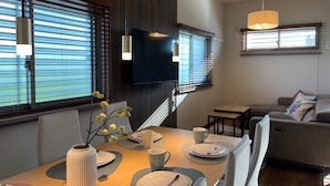 Uma sala de jantar moderna com uma mesa posta para quatro pessoas, uma televisão na parede e um ventilador de teto.
