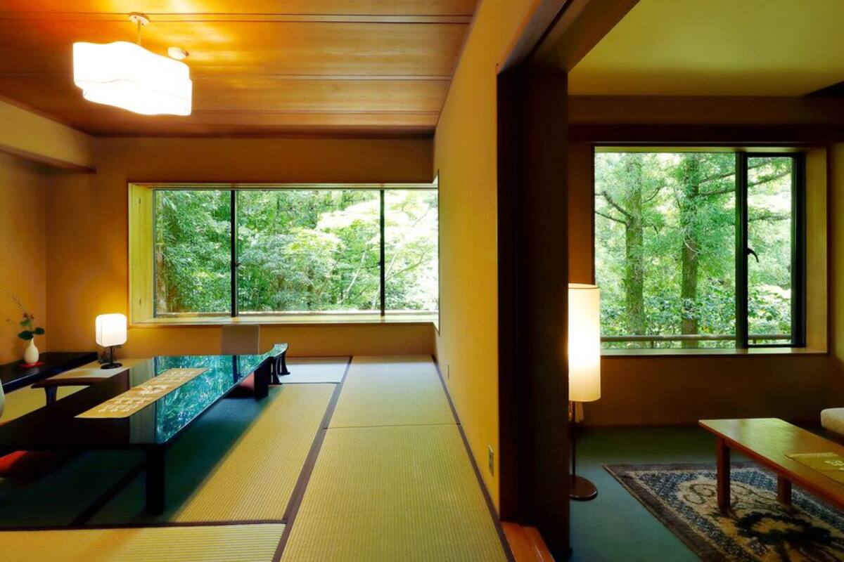 Um quarto com tatame e vista para árvores, uma escrivaninha e uma cadeira.