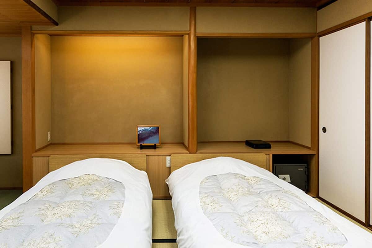 Quarto com duas camas, uma cadeira, uma mesinha e um armário.