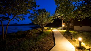 Caminho noturno que leva a um edifício com vista para um lago e montanhas.