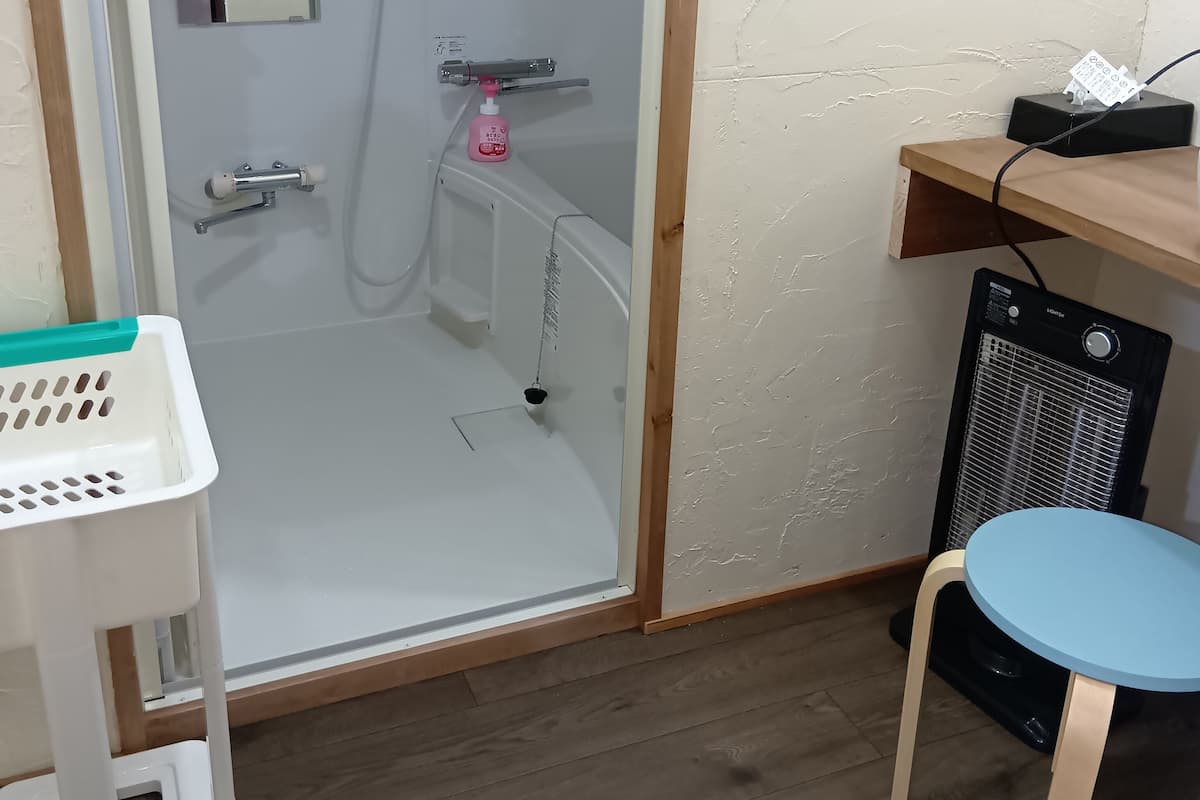 Área de duche com porta de vidro, pia branca, um banquinho azul e aquecedor no chão.