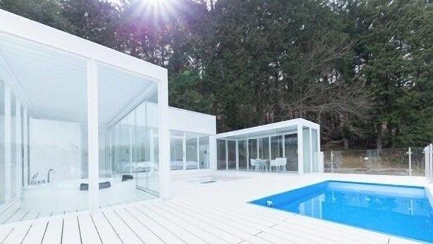 Uma área de piscina ao ar livre moderna, com deck de madeira, assentos envidraçados e vista desobstruída das árvores ao redor.