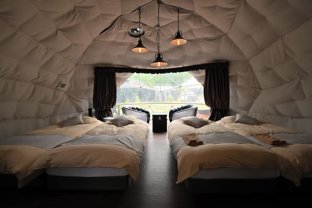 Um quarto em estilo de tenda com duas camas, uma mesa e luminárias pendentes.