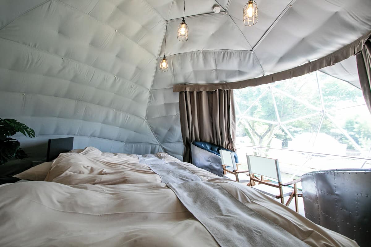 Um quarto tipo tenda aconchegante e bem iluminado, com uma cama, uma escrivaninha e uma cadeira.