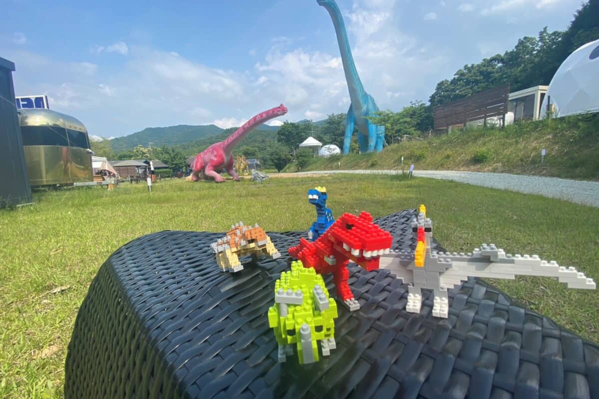 Uma área gramada com uma superfície preta trançada, uma grande escultura de dinossauro azul e uma escultura de dinossauro vermelha.
