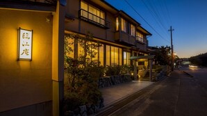 Um edifício japonês tradicional com uma placa, um caminho de pedra e uma entrada bem iluminada.