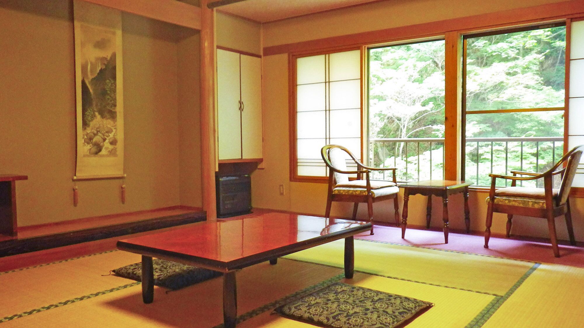Um quarto japonês tradicional com tatames, uma mesa baixa, duas cadeiras, um armário e uma janela grande com vista para o verde.