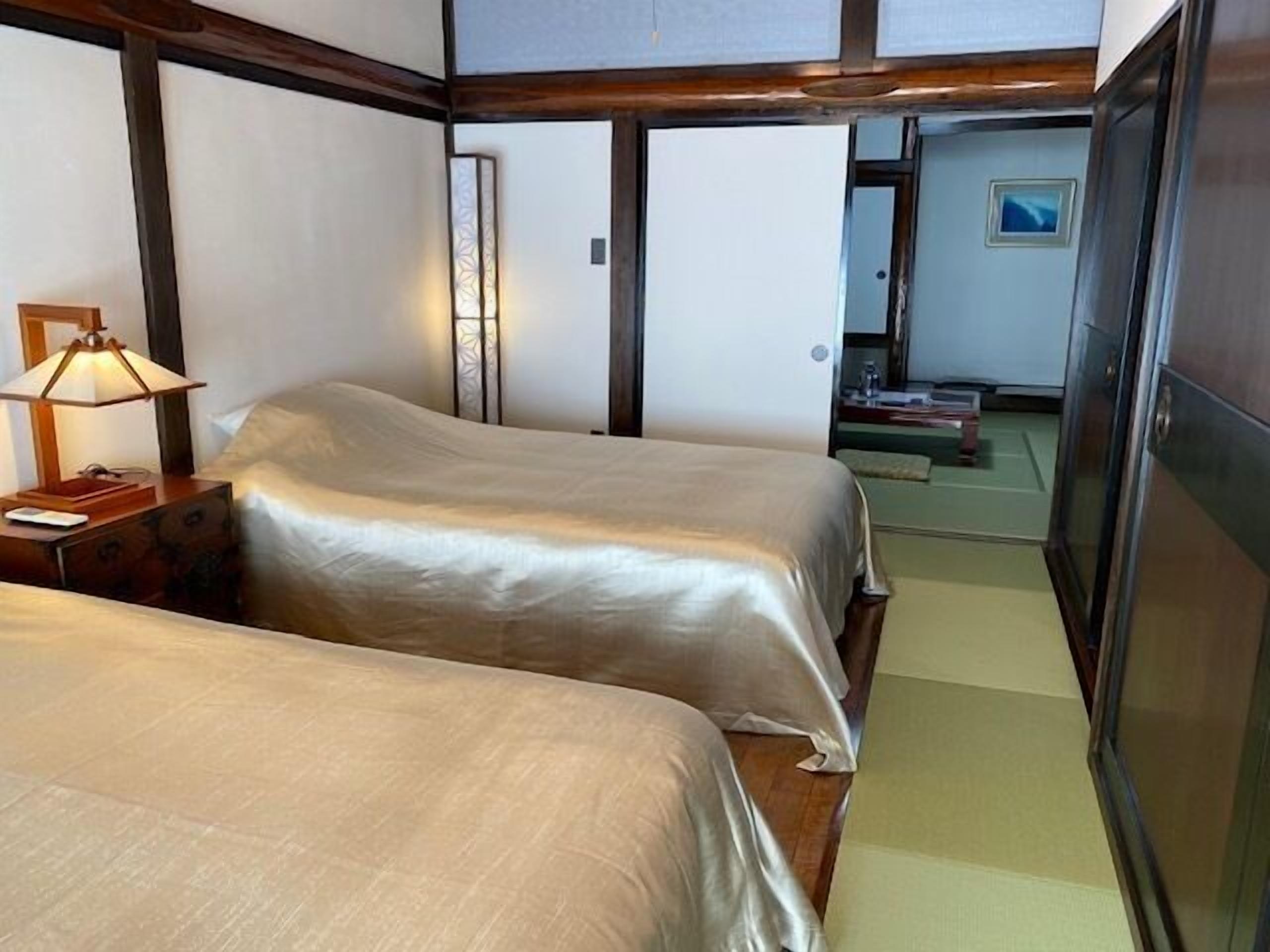Quarto com duas camas, uma mesa de cabeceira com abajur e uma porta de correr para outro espaço.