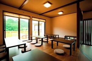Um espaço com várias mesas e bancos, grandes janelas e vista para o verde lá fora.