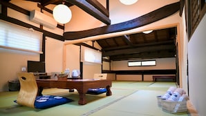 Um quarto japonês tradicional com tatames, uma mesa de madeira baixa, uma cadeira acolchoada e uma pequena escrivaninha de madeira com um computador.