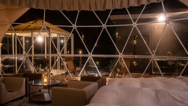 Um espaço coberto por uma tenda com teto de vidro, várias áreas de estar e vista para o céu noturno.