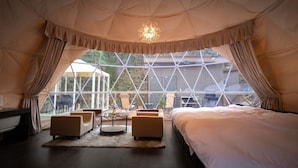 Um quarto tipo tenda com uma cama, dois sofás, uma mesinha e um lustre.