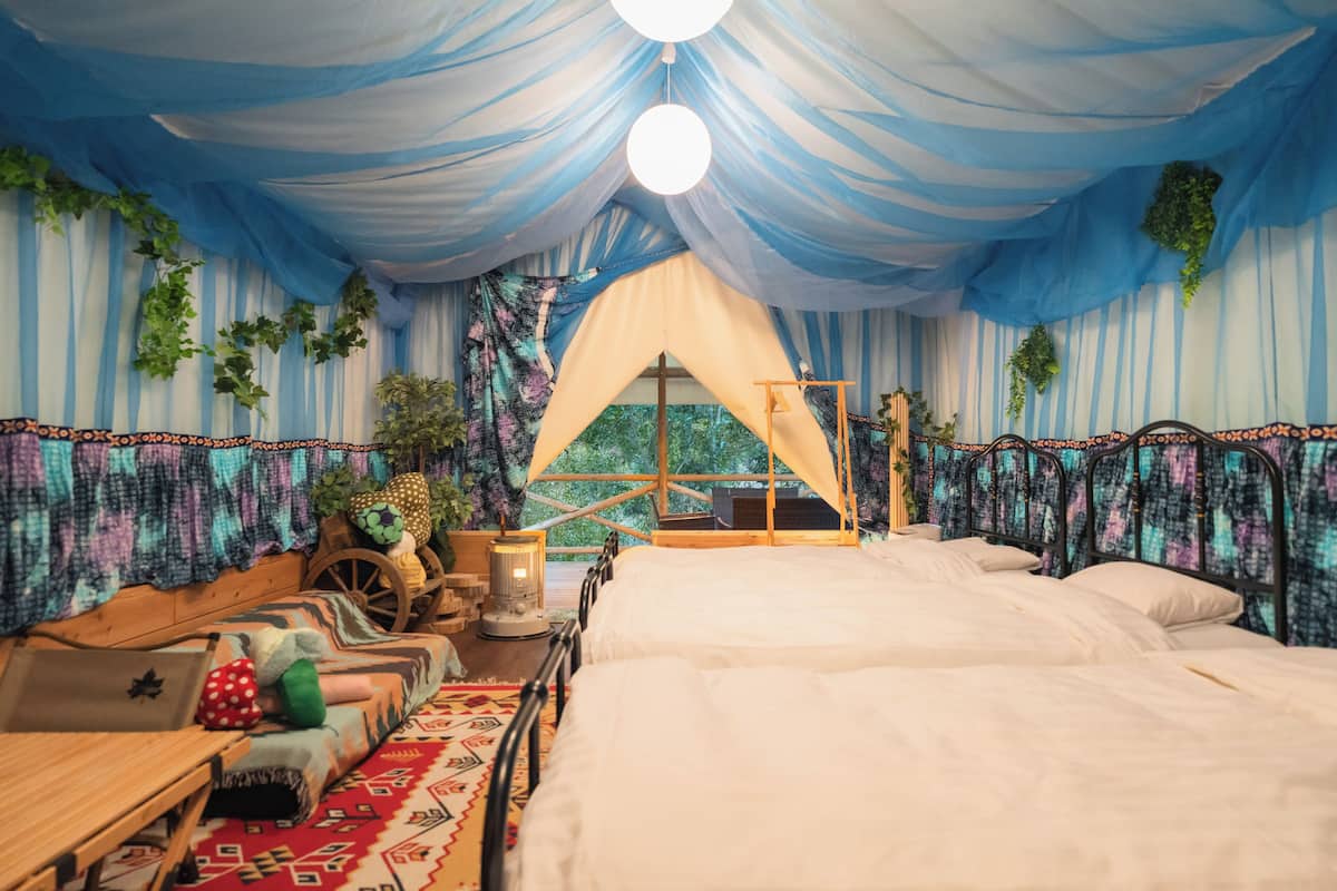 Quarto com tenda, duas camas, um banco de madeira, uma mesa e vista para o verde lá fora.