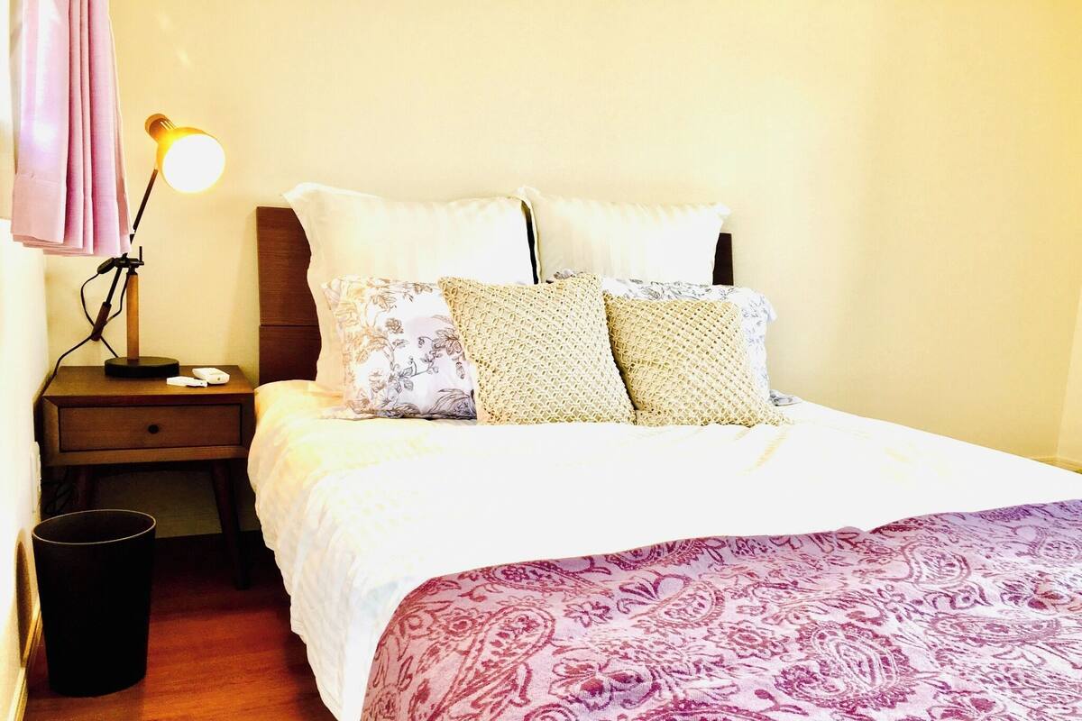 Uma cama bem arrumada com colcha estampada, dois travesseiros, uma luminária de cabeceira e uma mesa de cabeceira com gaveta.