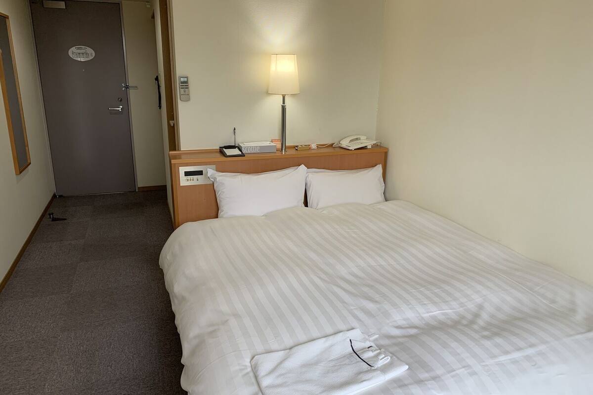 Quarto de hotel com cama, abajur, telefone e porta.