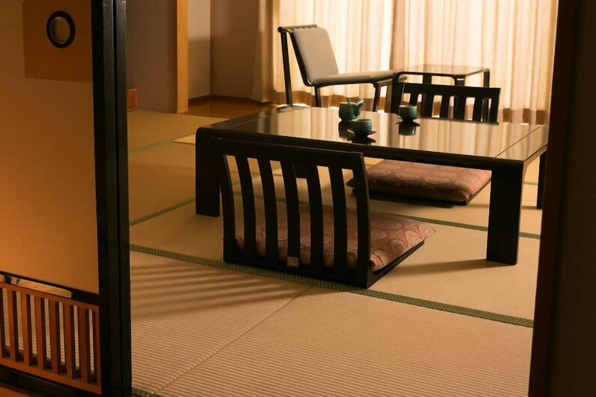 Um quarto japonês tradicional com esteiras de tatame, uma mesa baixa, cadeiras e um conjunto de chá.