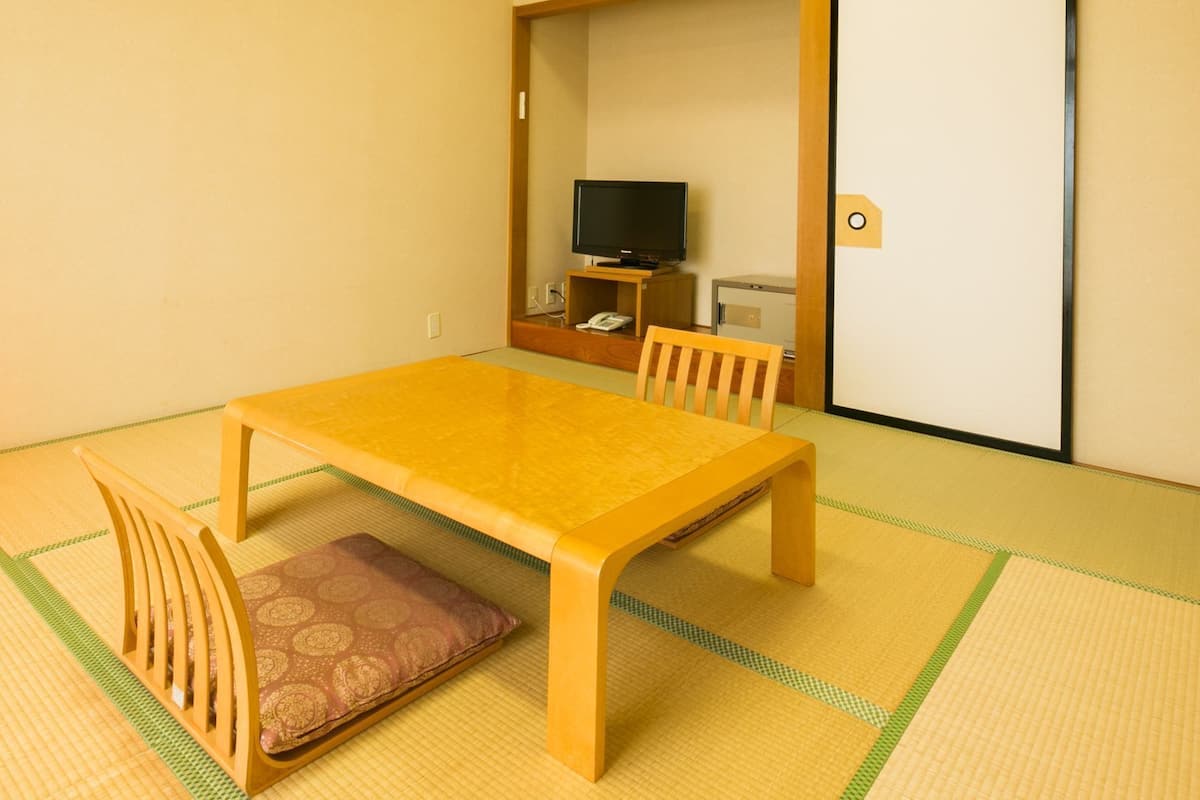Quarto com piso de tatame, uma mesa de madeira com assento, uma cadeira, uma televisão e um armário.