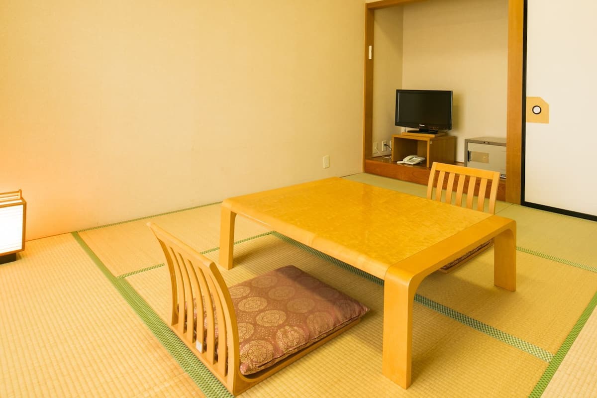 Quarto com piso de tatame, uma mesa baixa, cadeira, almofada, televisão e um armário.