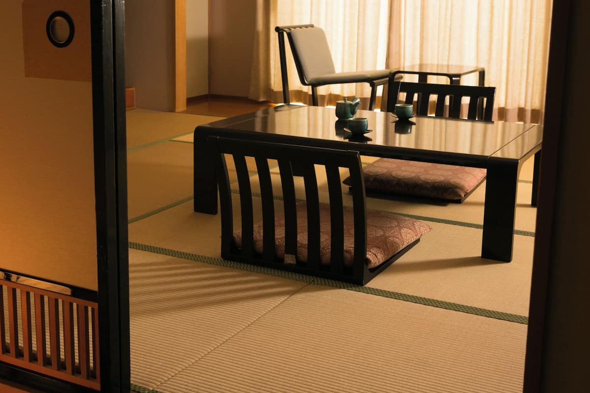 Um espaço com tatames, uma mesa baixa e cadeiras, um conjunto de chá e um separador shoji.