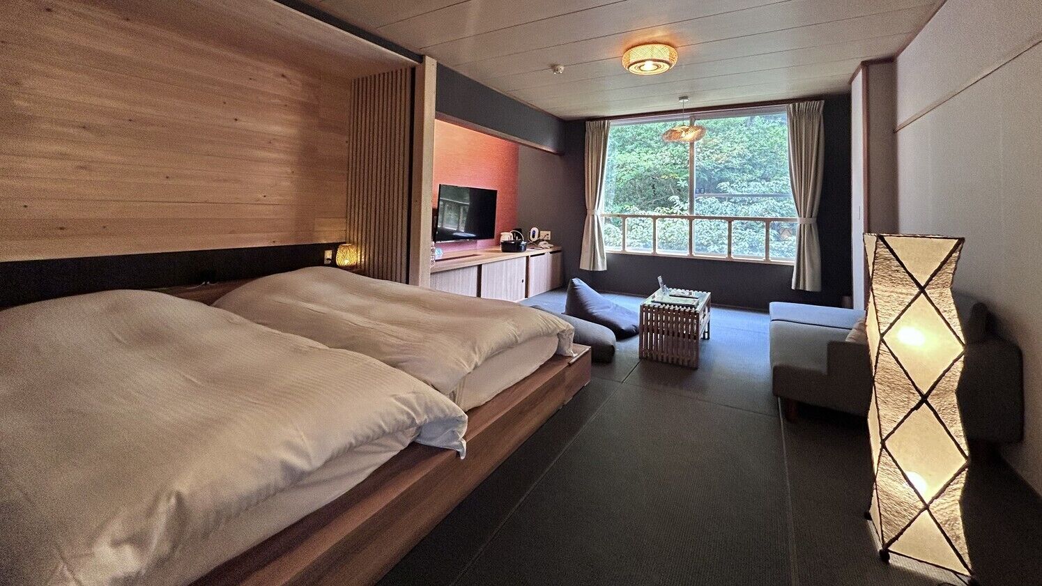 Quarto com uma cama grande, uma escrivaninha, uma cadeira e janela com vista para árvores.