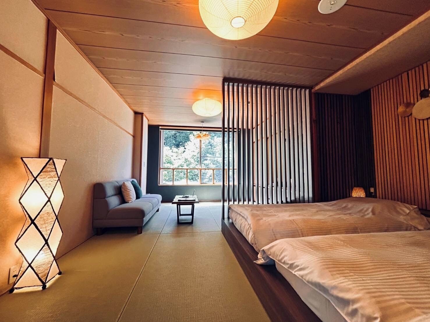 Quarto com sofá, cama, mesinha e janela com persianas verticais.