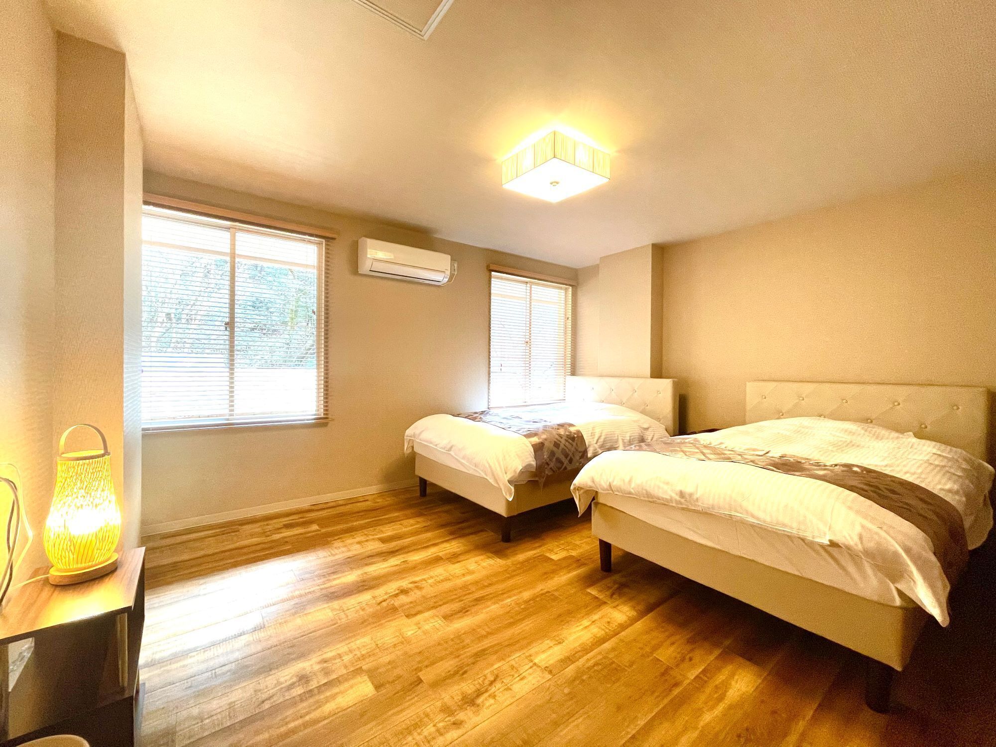 Quarto com duas camas, uma escrivaninha e um abajur.