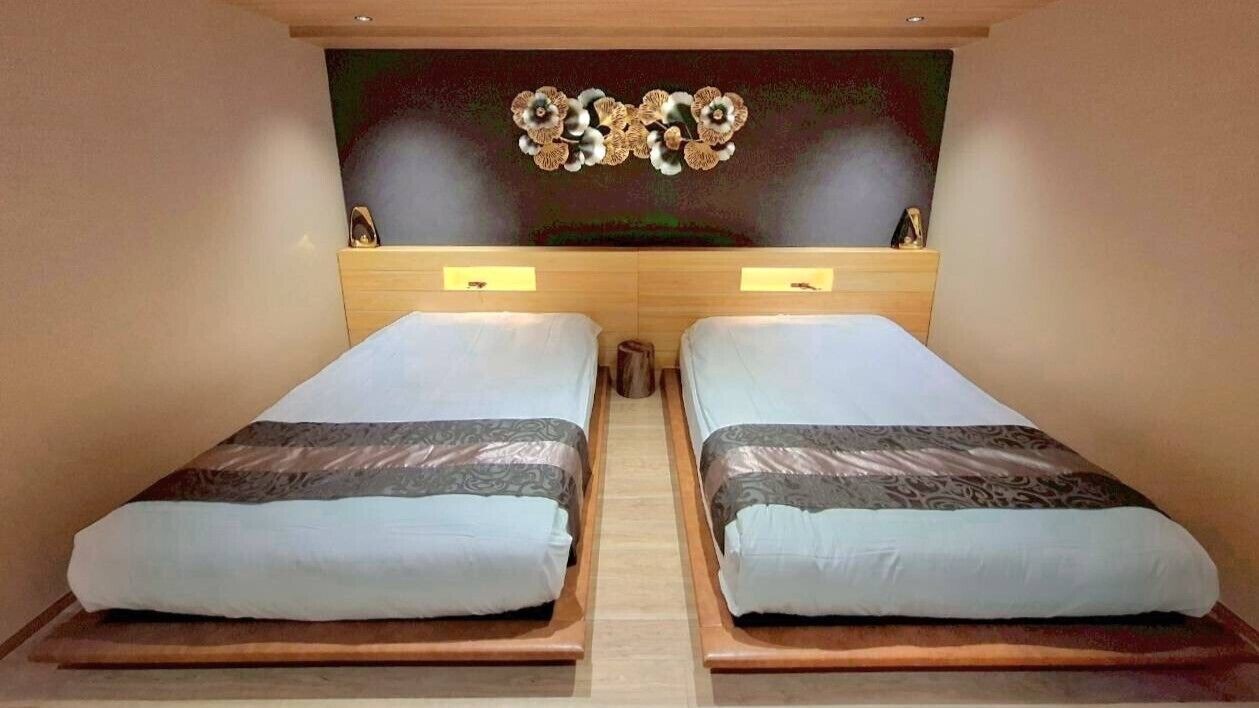 Quarto com cama de casal, peseira de madeira, duas mesas de cabeceira e um objeto decorativo sobre a cama.