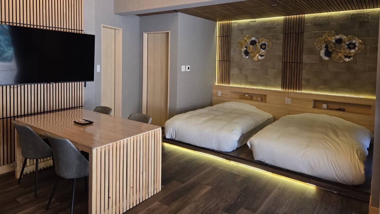 Quarto de hotel moderno com escrivaninha de madeira, duas camas, televisão de tela plana e arte decorativa na parede.