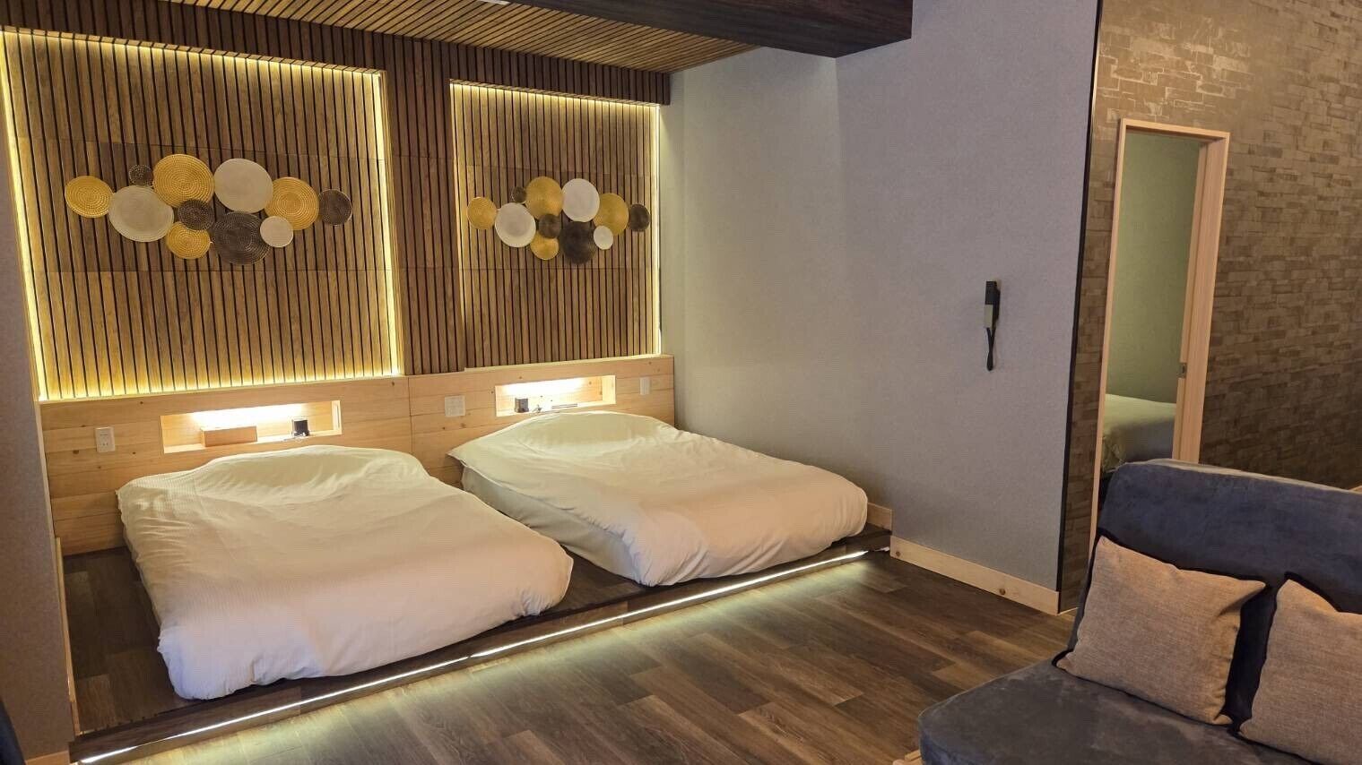 Quarto com duas camas, teto de madeira, parede com luminárias circulares e parede de tijolos.