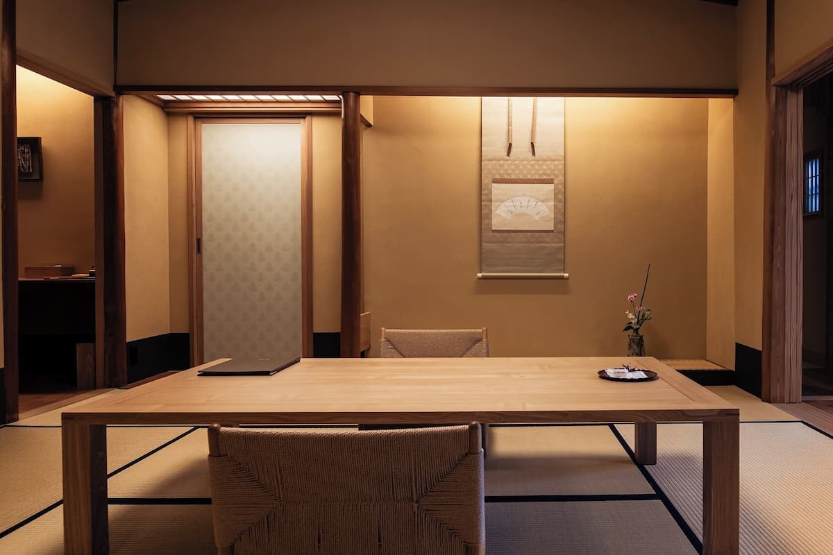 Quarto japonês tradicional com tatames, uma mesa baixa, uma cadeira e uma porta deslizante.