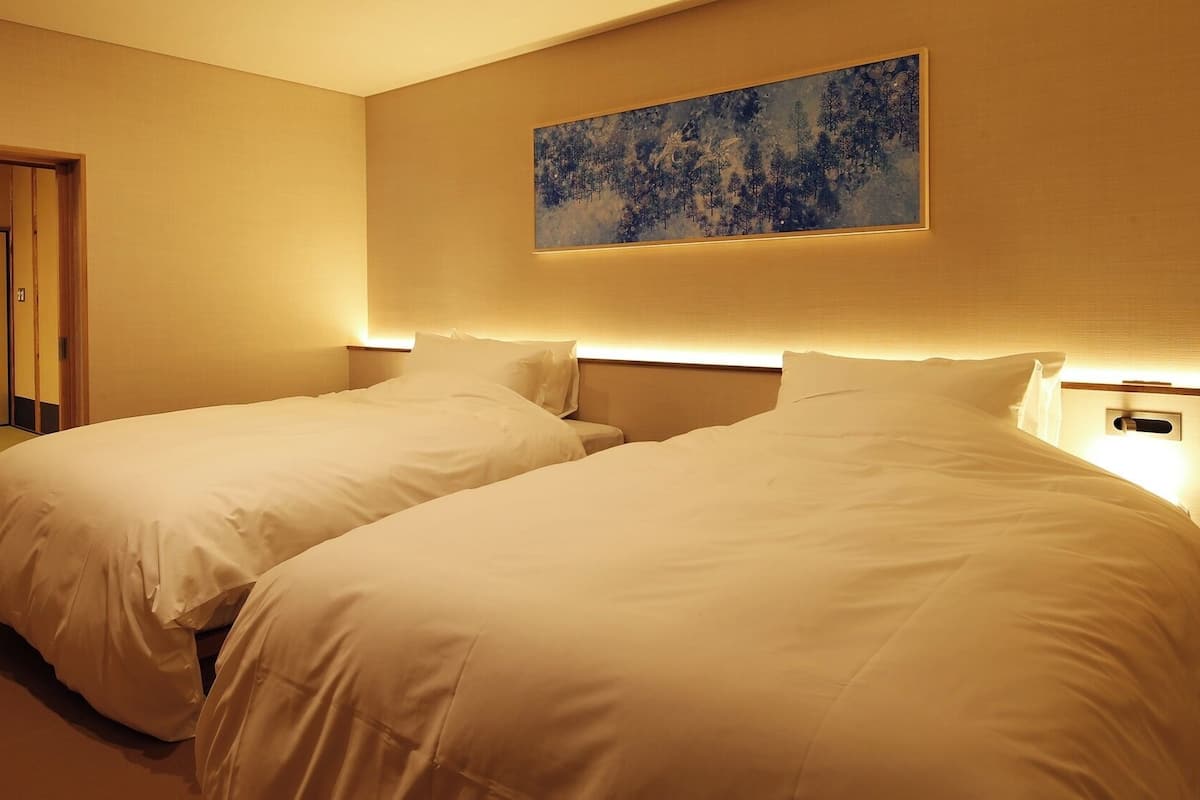 Quarto de hotel com duas camas, um quadro na parede e uma porta tradicional japonesa de correr.