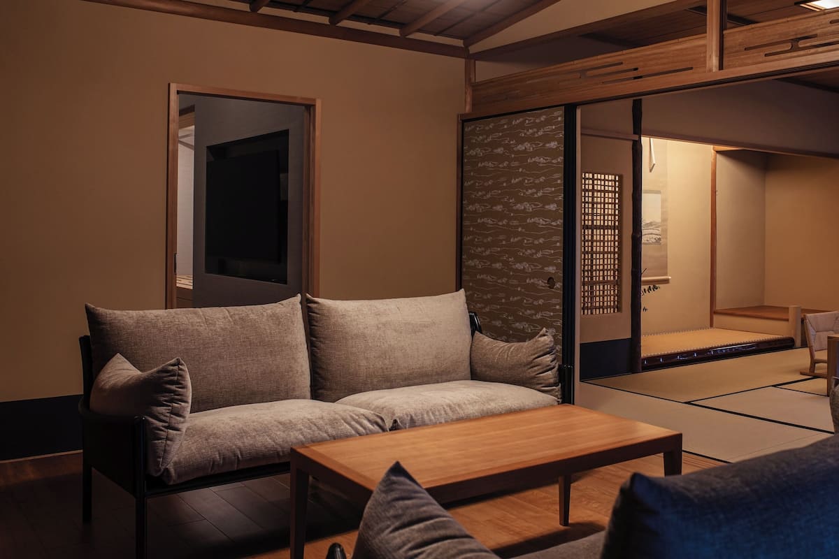 Quarto japonês tradicional com tatames, uma mesa de madeira baixa e um sofá com almofadas.