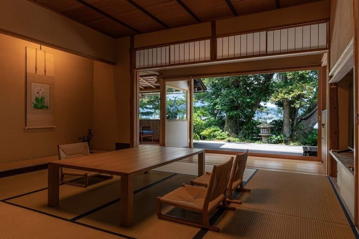 Um quarto japonês tradicional com piso de tatame, uma mesa baixa e cadeiras.